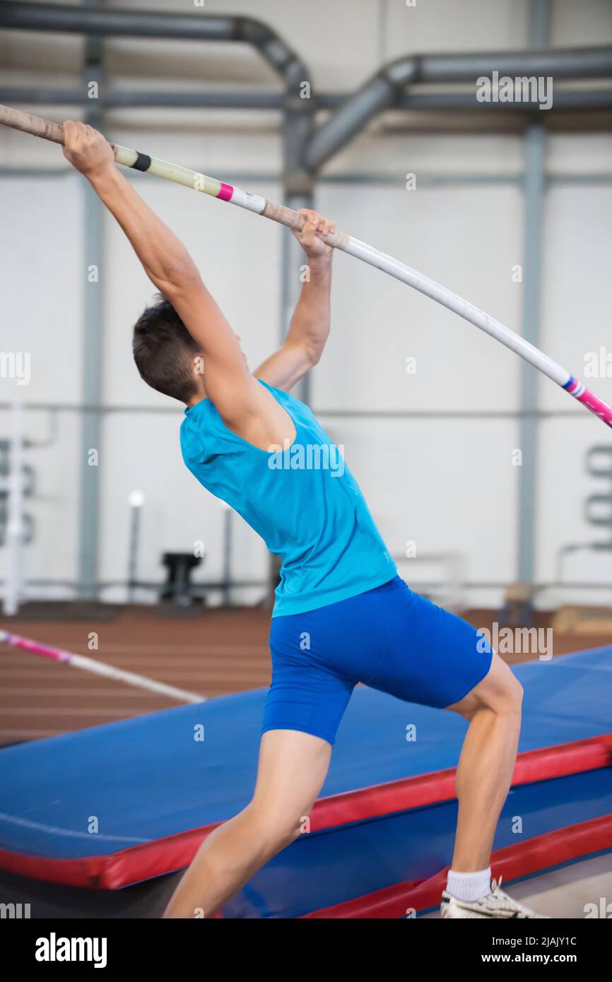 Pole vaulting indoors - young man leaning on the pole and about to jump ...