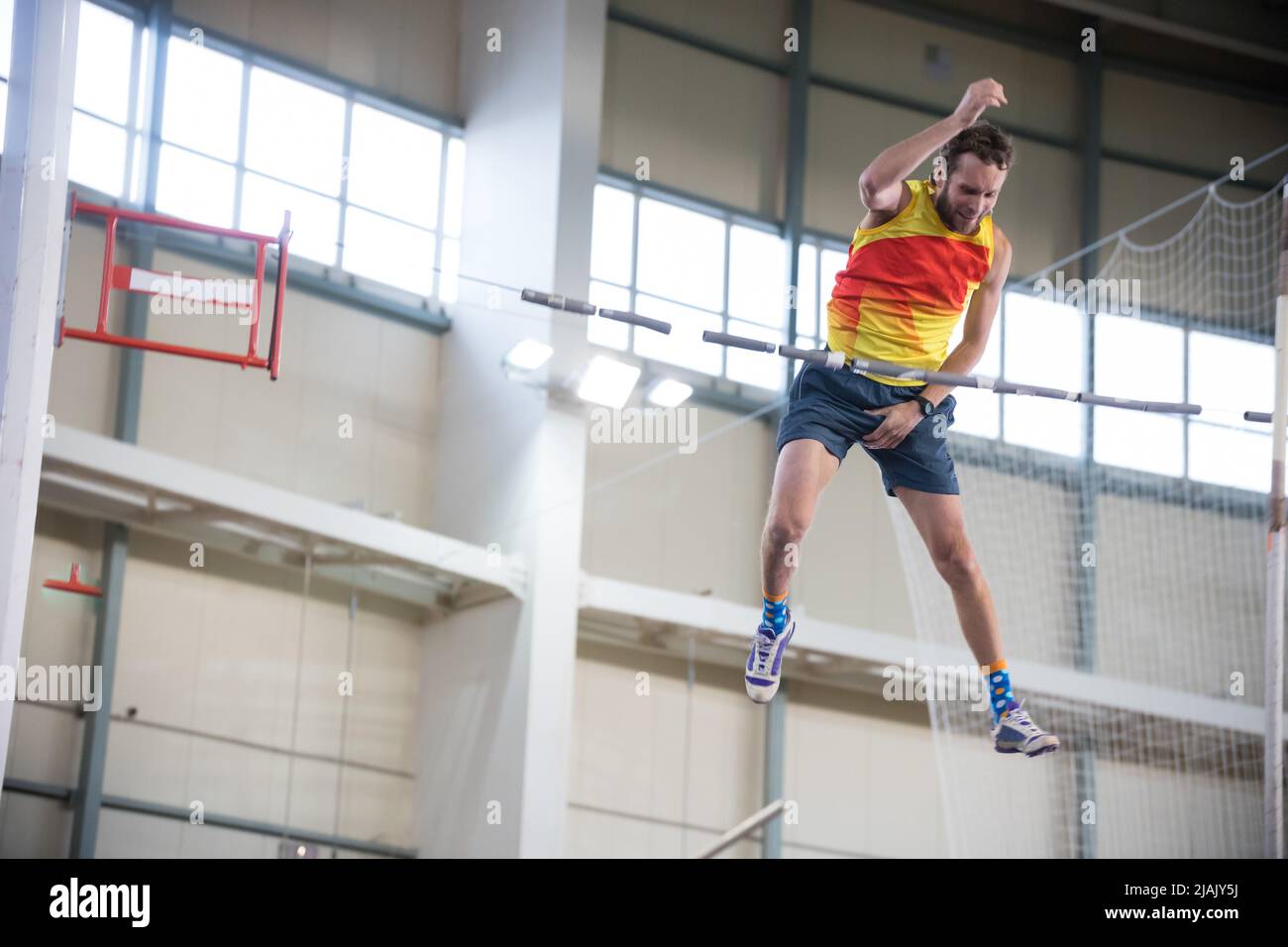 Pole vaulting indoors - a athletic man jumping over the bar and trying ...