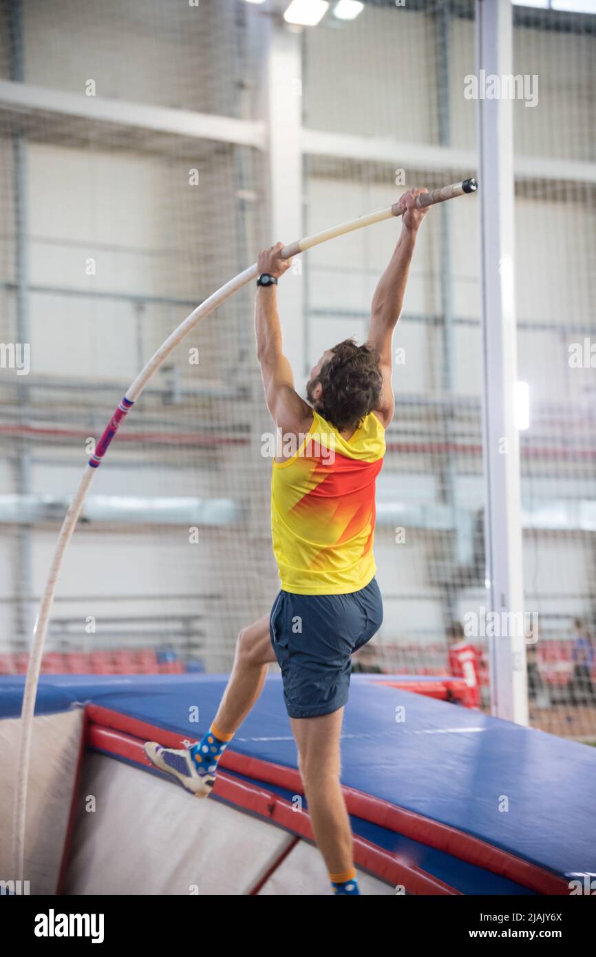 Pole vaulting indoors - a athletic man jumping over the bar - the pole ...