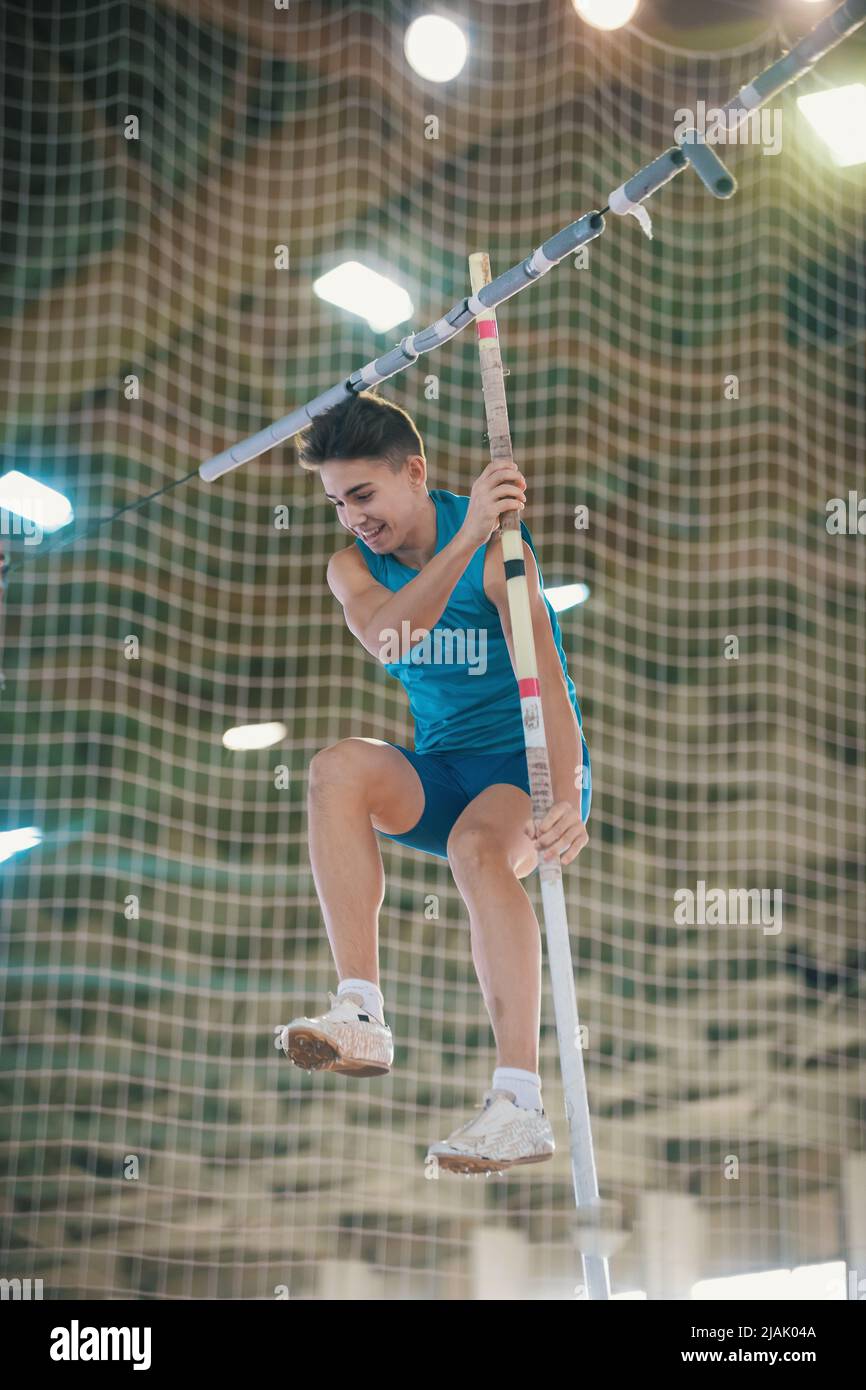 Pole vaulting indoors - young fit smiling man jumping leaning on the ...