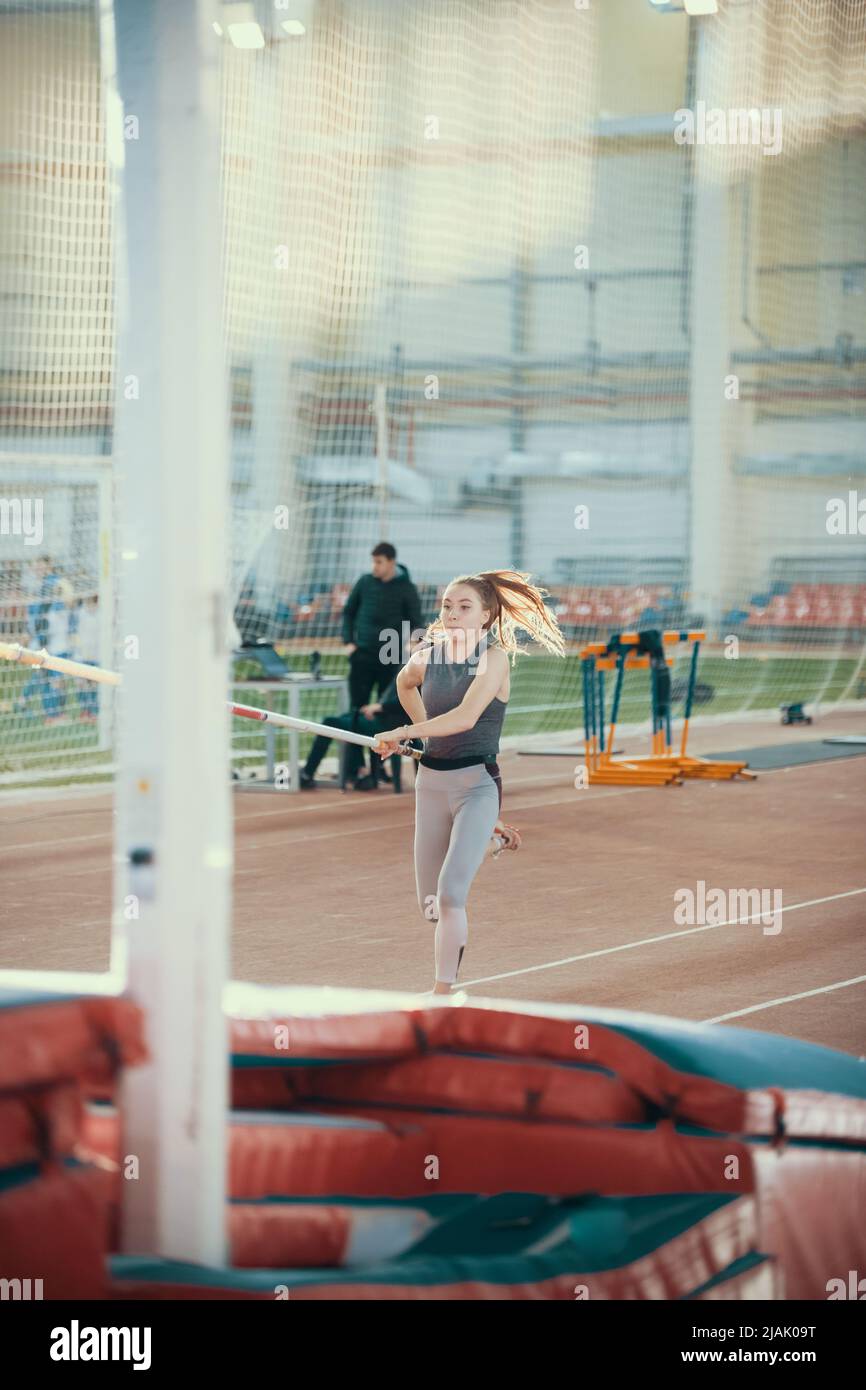 Pole vaulting indoors - young sportive woman with ponytail running with ...