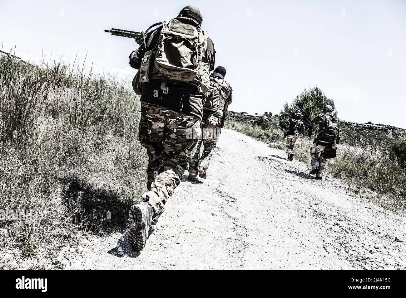 Soldiers running down a countryside road aiming their weapons towards ...