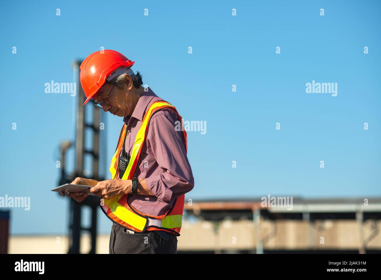 A senior elderly Asian worker engineer wearing safety vest and helmet ...