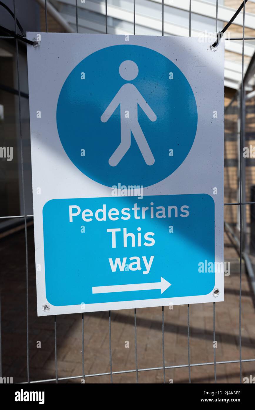Blue and white pedestrians this way sign with arrow hanging on metal ...