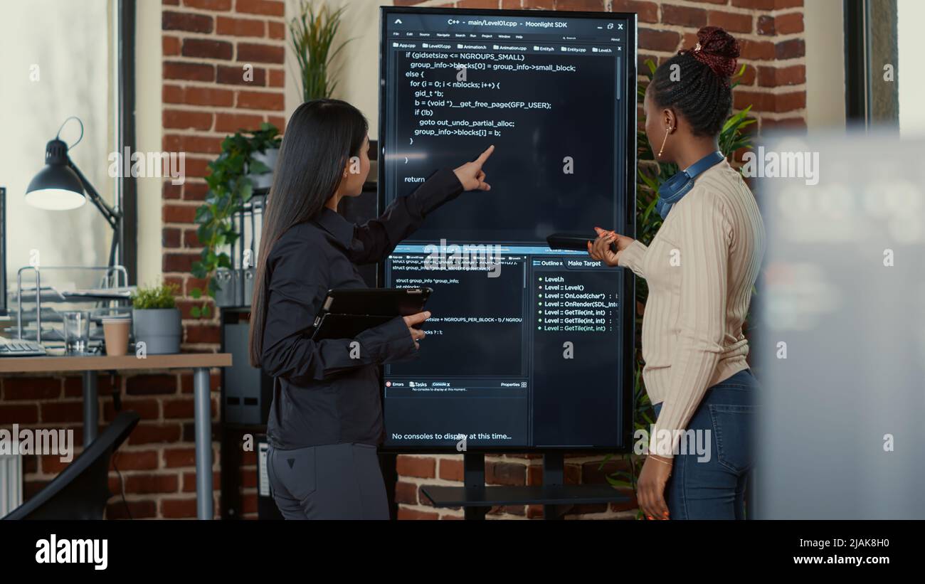 Team Of Programmers Analyzing Code On Wall Screen Tv Looking For Bugs And Errors While Holding