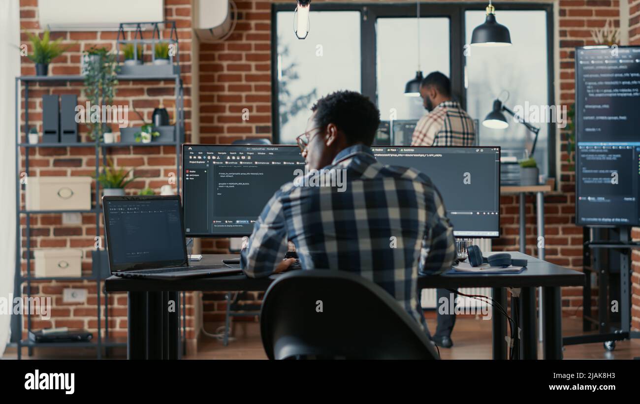 Programer Coding On Laptop Sitting Down At Desk With Computer Screens Parsing Code In Software
