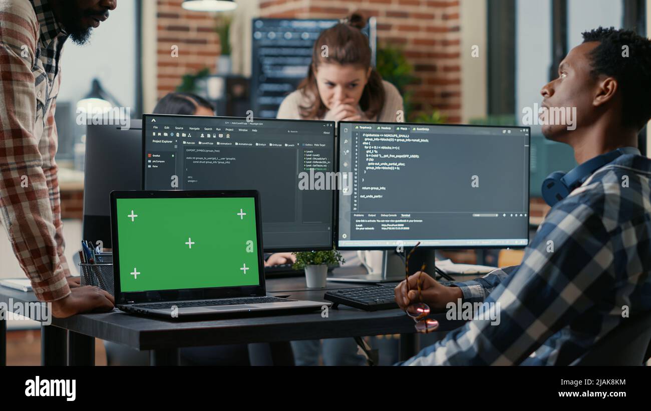 Programer taking glasses off talking with colleague at desk with laptop ...