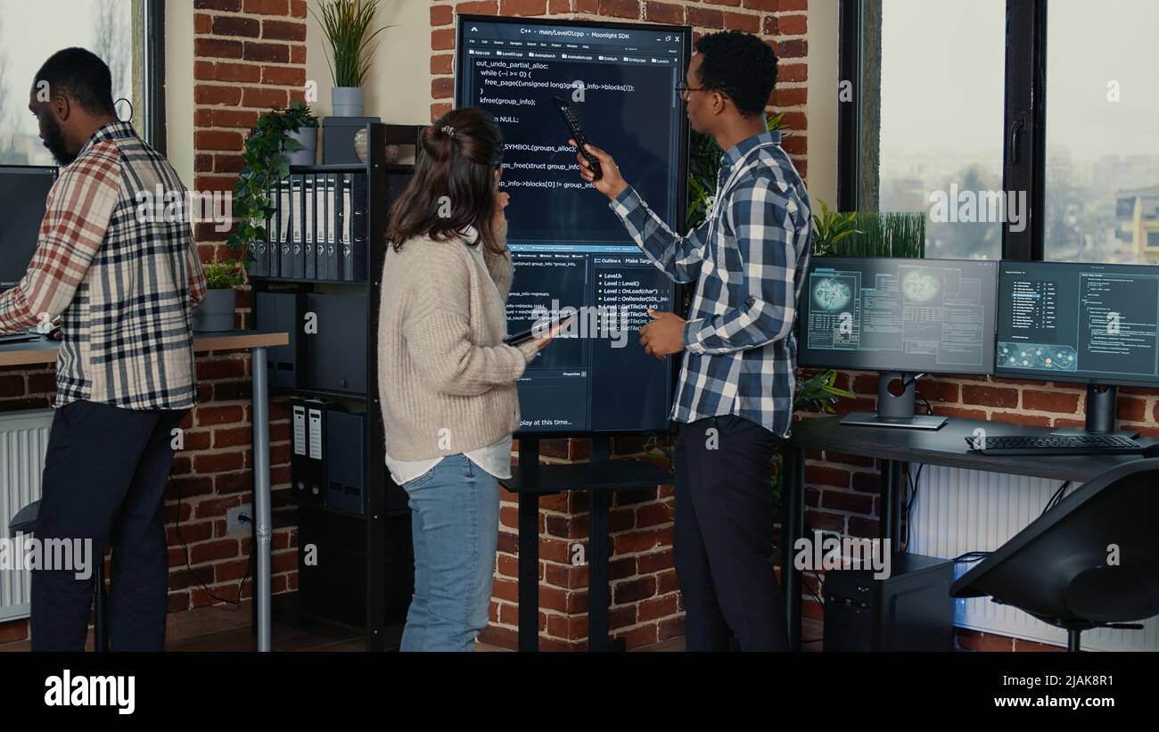 Team Of Database Admins Analyzing Source Code On Wall Screen Tv Comparing Errors Using Digital