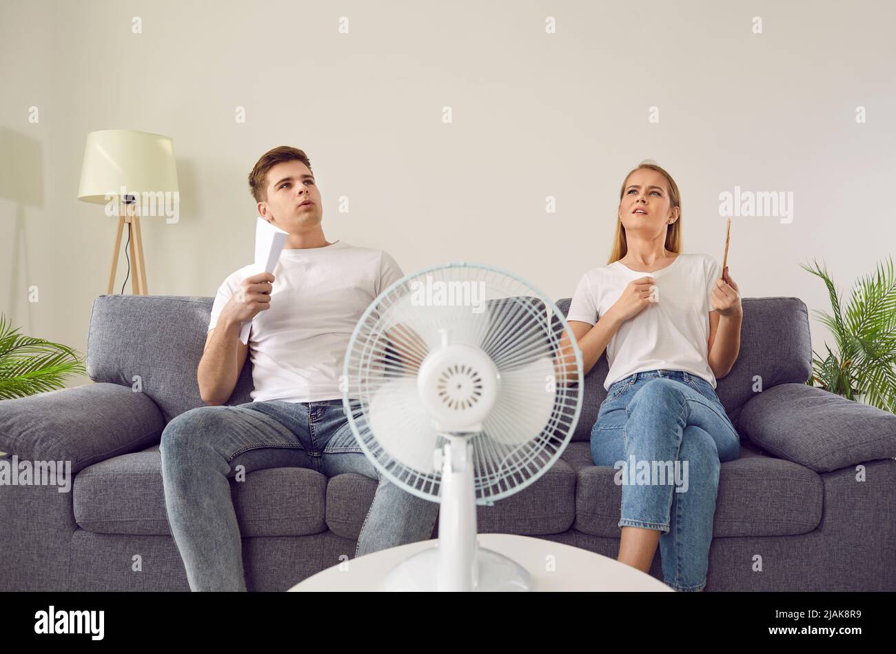 Young couple suffering from hot summer weather and sitting on sofa with ...