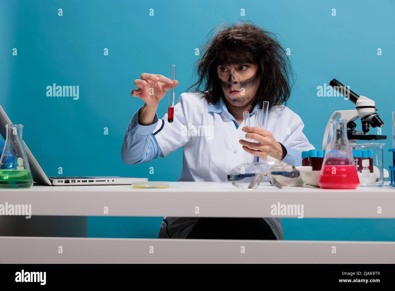 Foolish crazy looking mad chemist sitting at desk in laboratory while ...