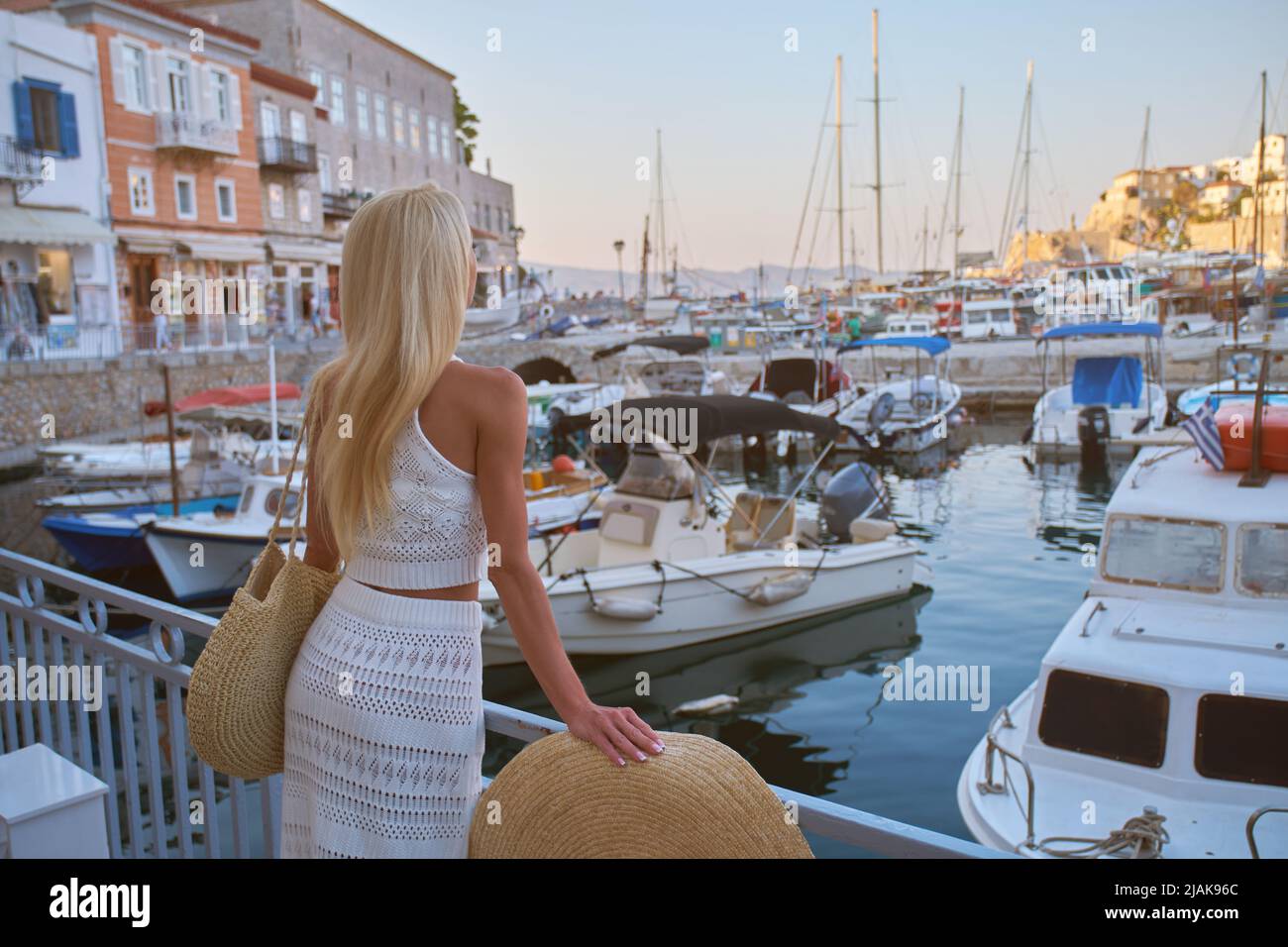 Young lady wearing dress and straw hat walking in marina. Greece, Hydra ...