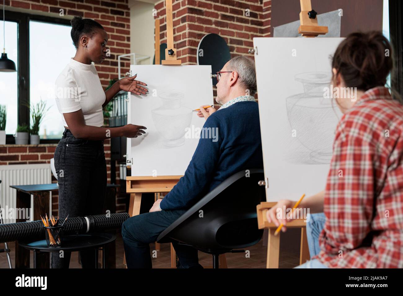 Young painter teacher explaining sketching technique to elderly student ...