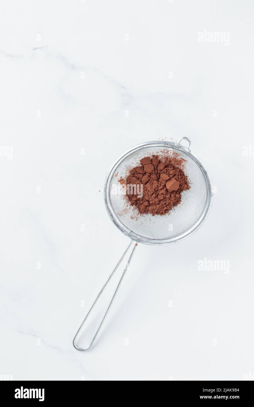 Cocoa powder sweet ingredient in a strainer on a white backround top ...