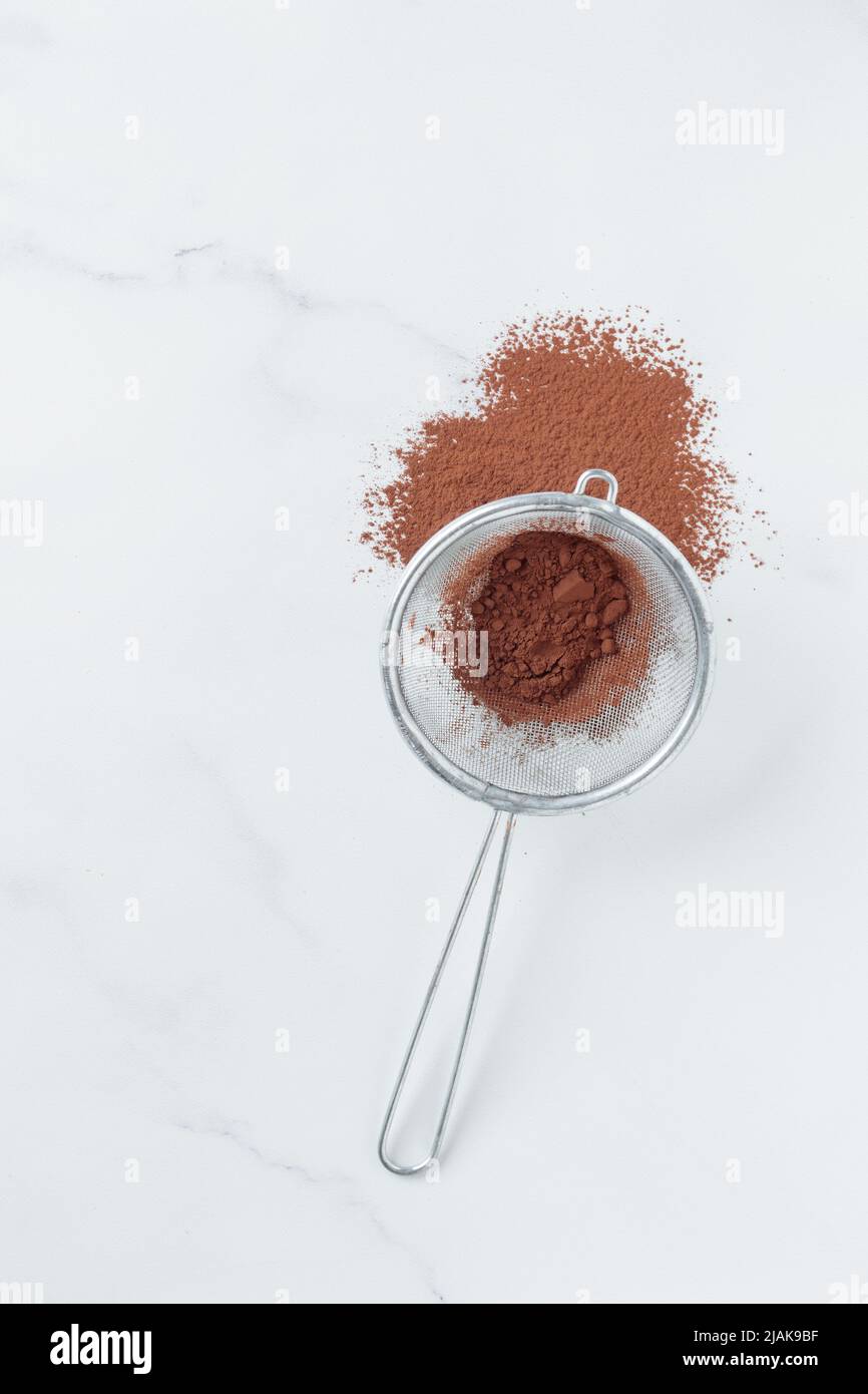 Cocoa powder sweet ingredient in a strainer on a white backround top ...