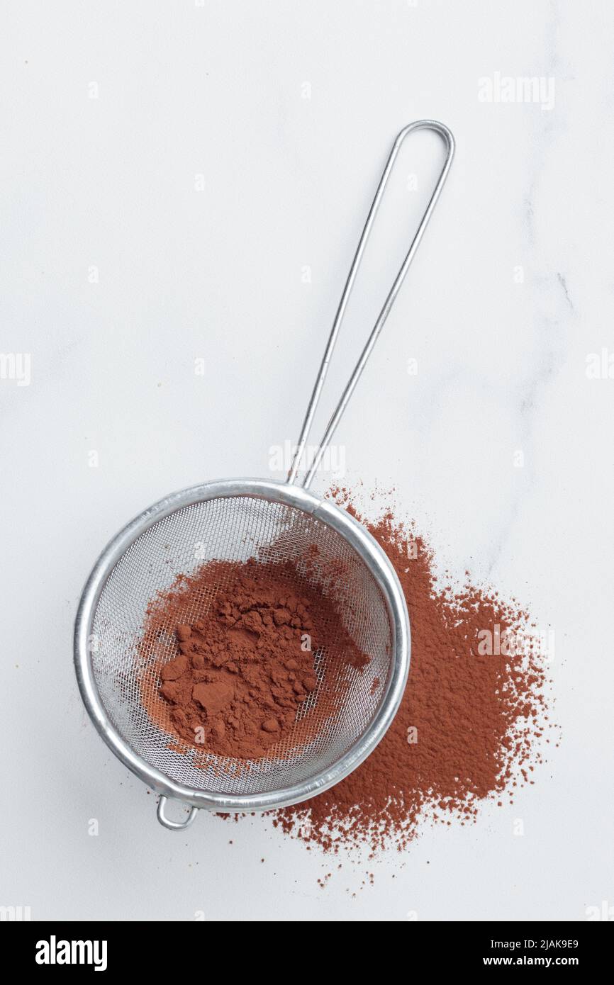Cocoa powder sweet ingredient in a strainer on a white backround top ...