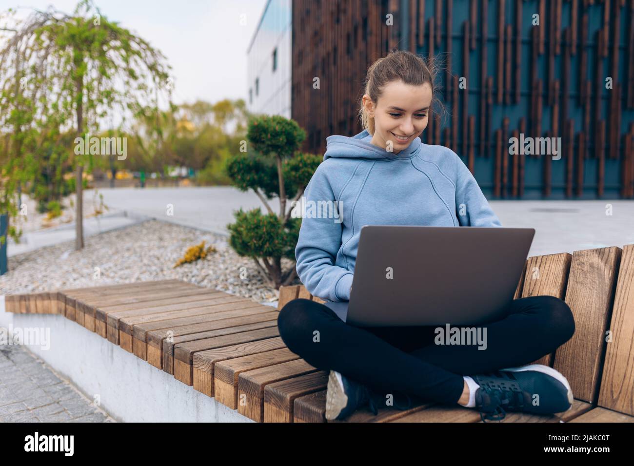 Girl sitting with crossed legs on bench, holding laptop Stock Photo - Alamy