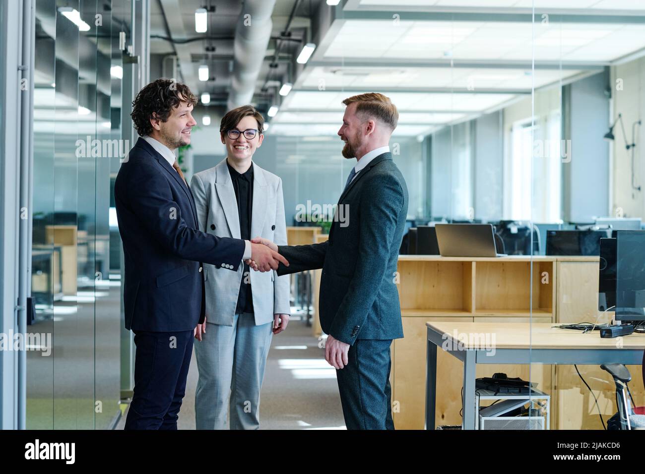 Business partners in formal suits greeting each other before meeting with young businesswoman ...