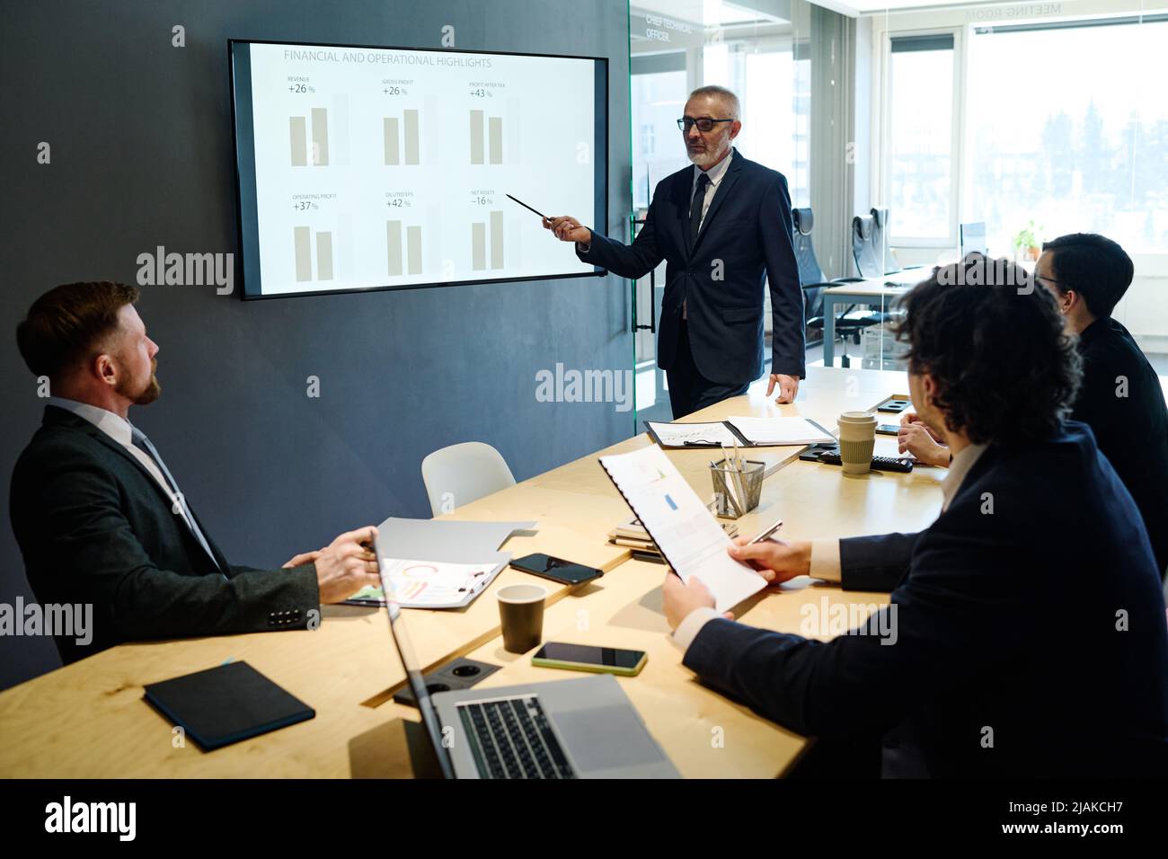Mature businessman in suit pointing at screen display with graphs and ...