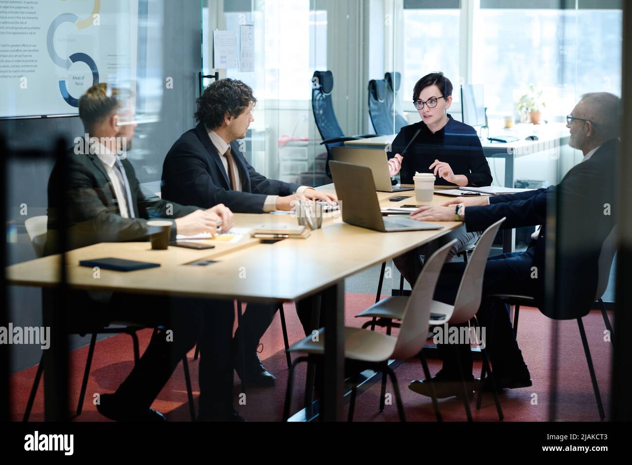 Group of business people sitting at table with computers and discussing ...