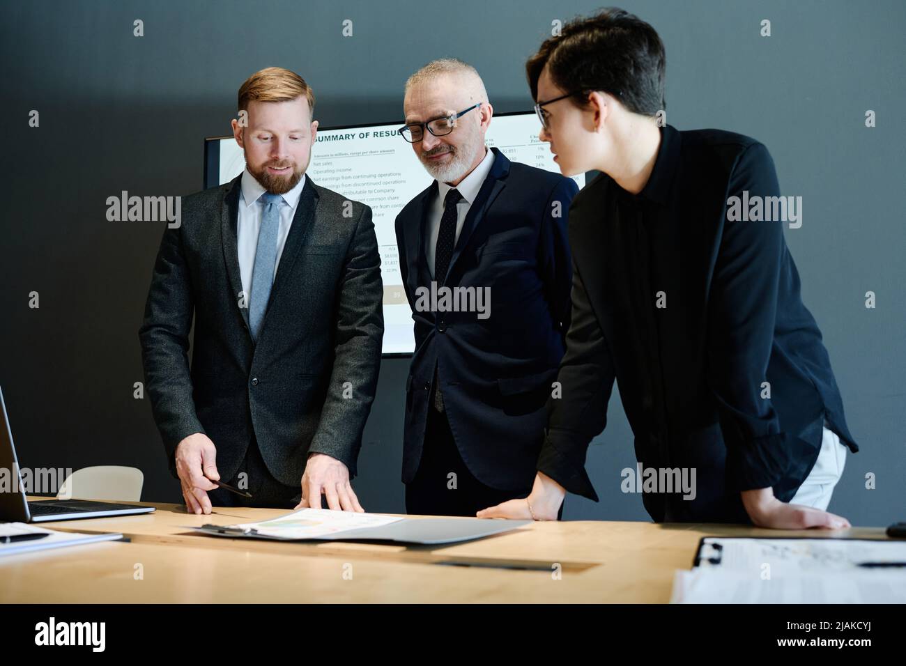 Business partners in formal suit looking at report at table and ...
