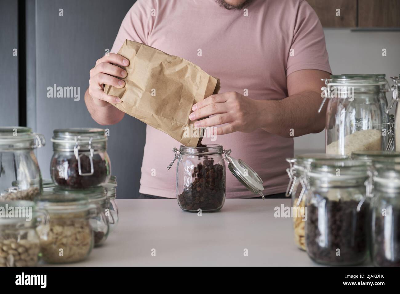Unrecognizable latin man filling up a jar with raisins from a paper bag ...