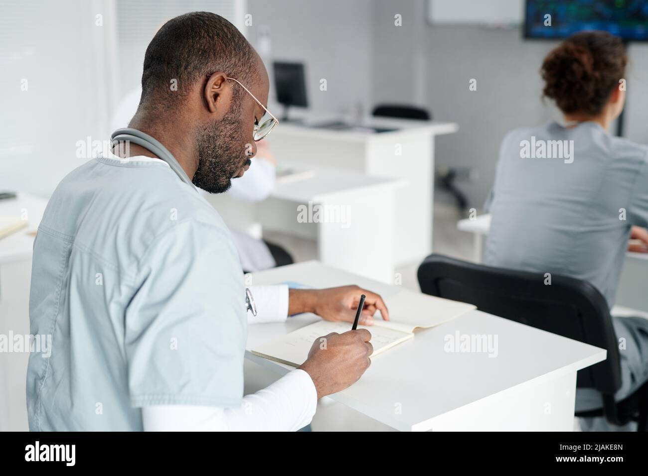 Rear view of African male doctor in uniform writing in notebook at desk ...