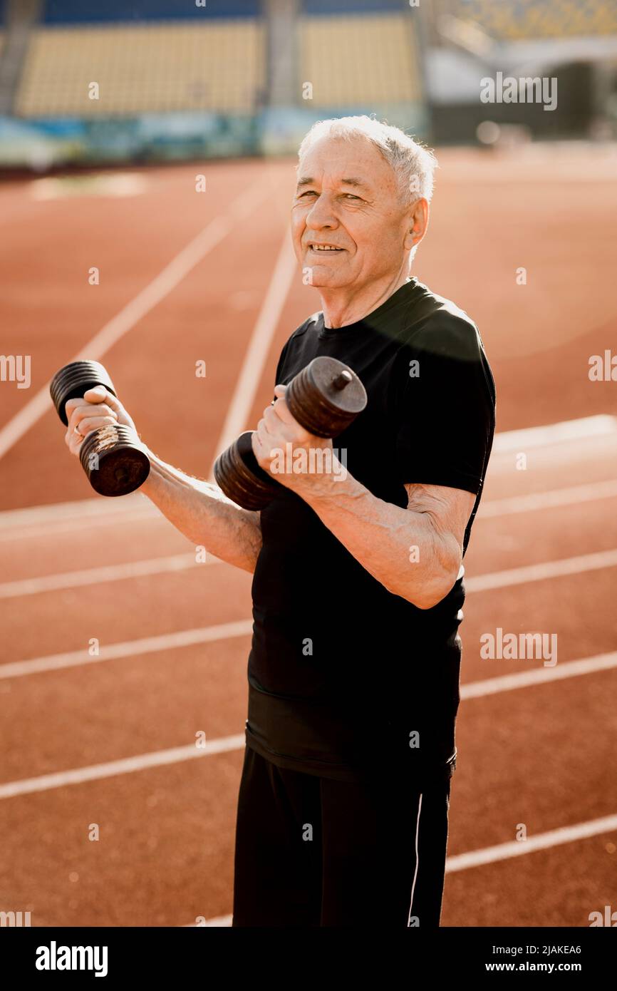 Handsome old man doing exercise with dumbbells in black sportswear ...