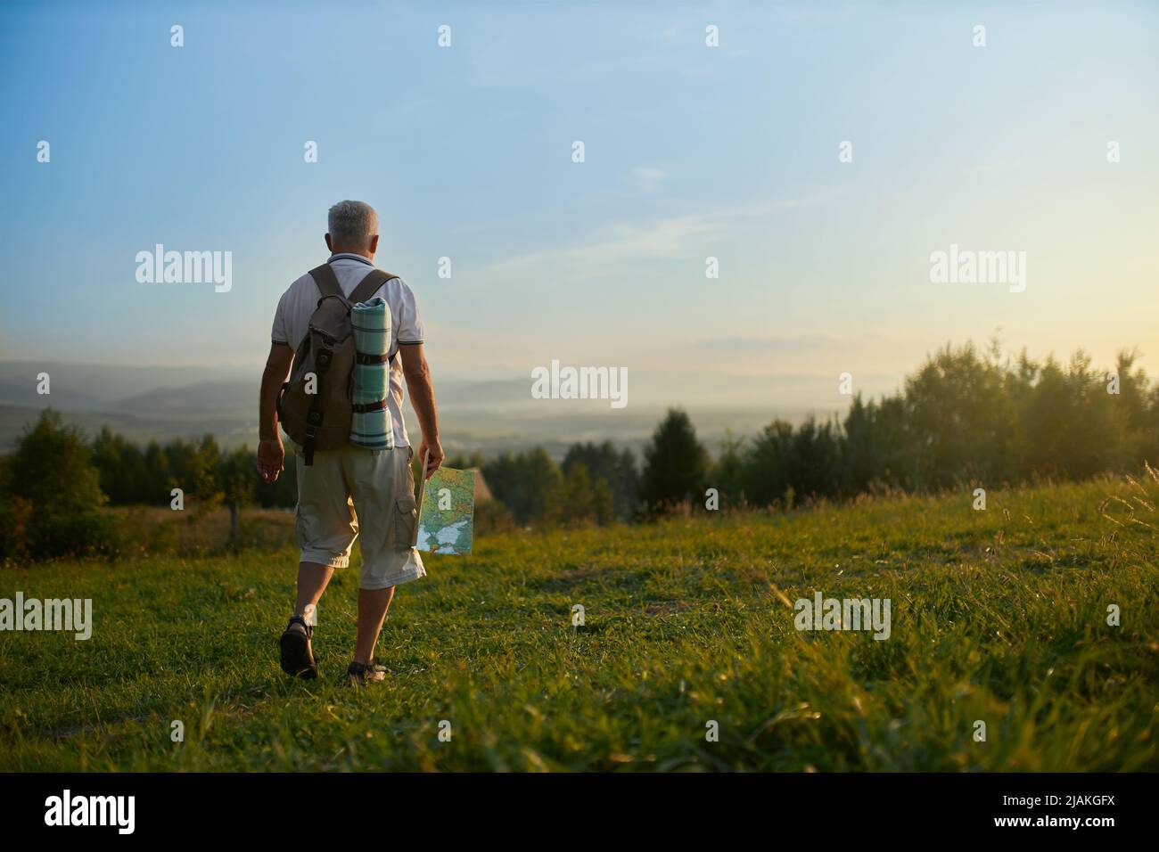 Middle aged man walking down hill, while hiking in mountains. Back view ...