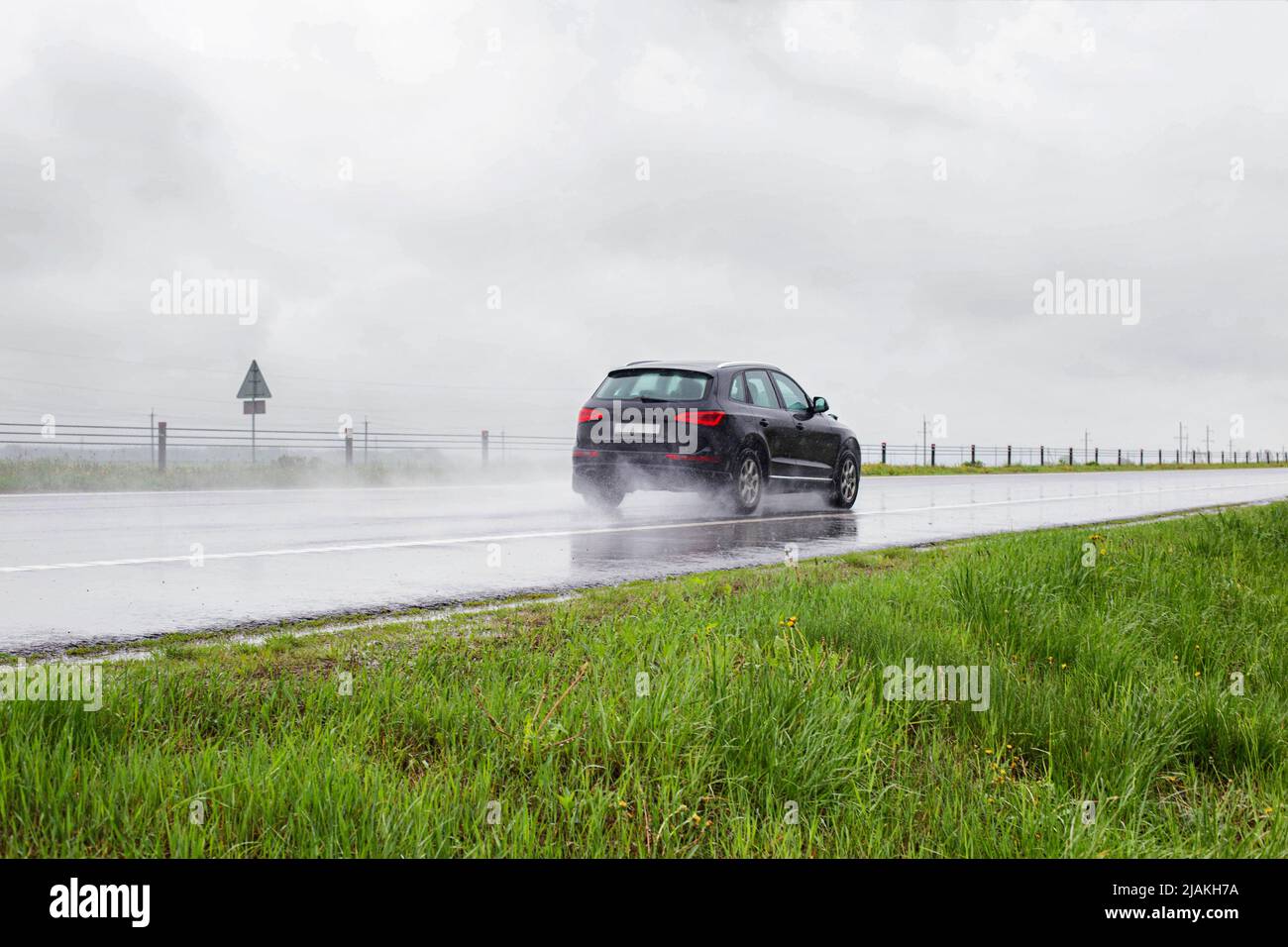 A modern black crossover car rides on a wet road in the rain in summer ...