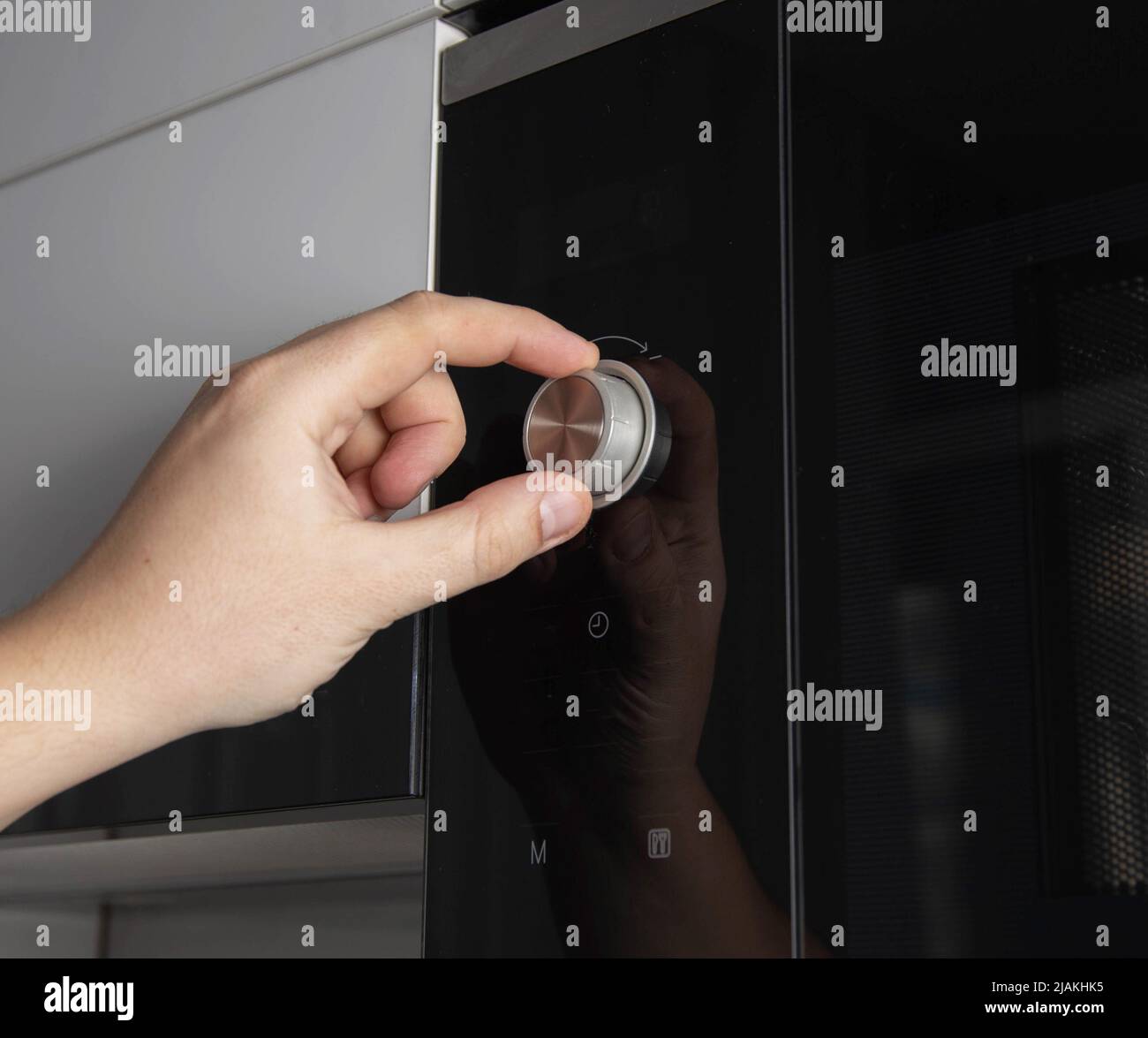 A man's hand twists a regulator button on a modern microwave oven panel ...