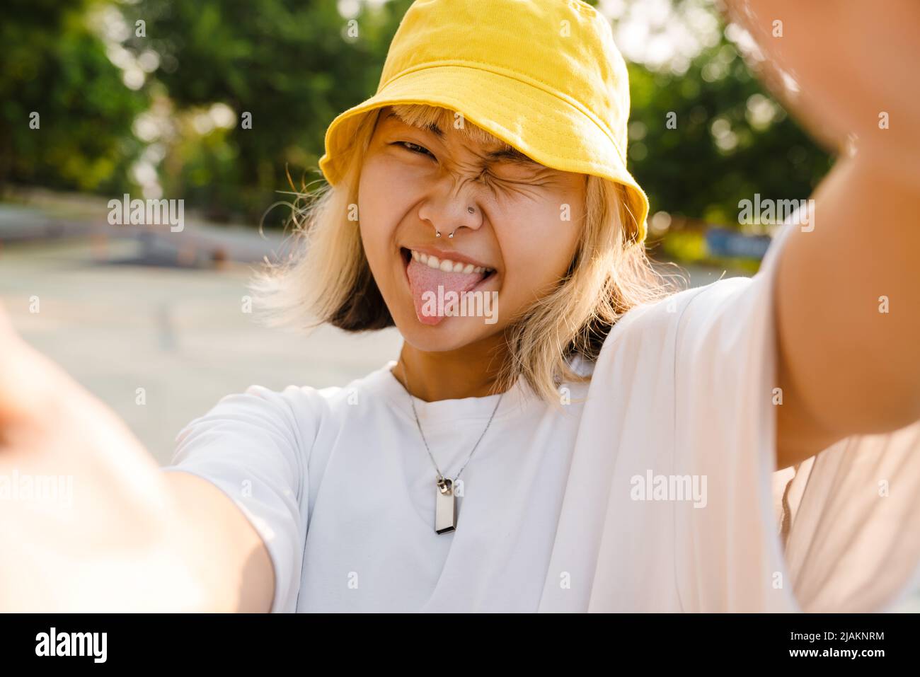 Asian Girl Winking And Showing Her Tongue While Taking Selfie Outdoors