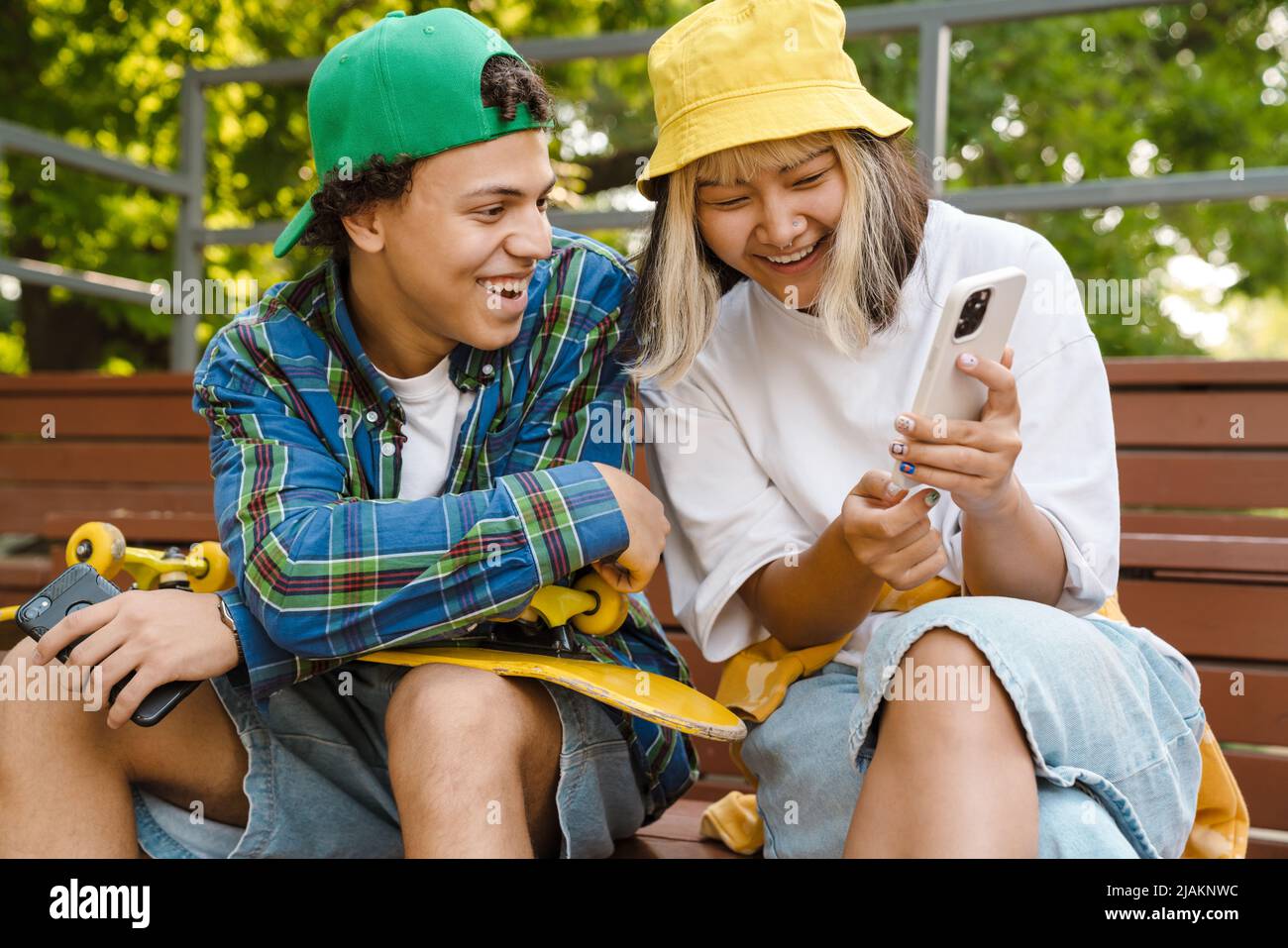 Two multiracial teenagers smiling and using cellphone while spending ...