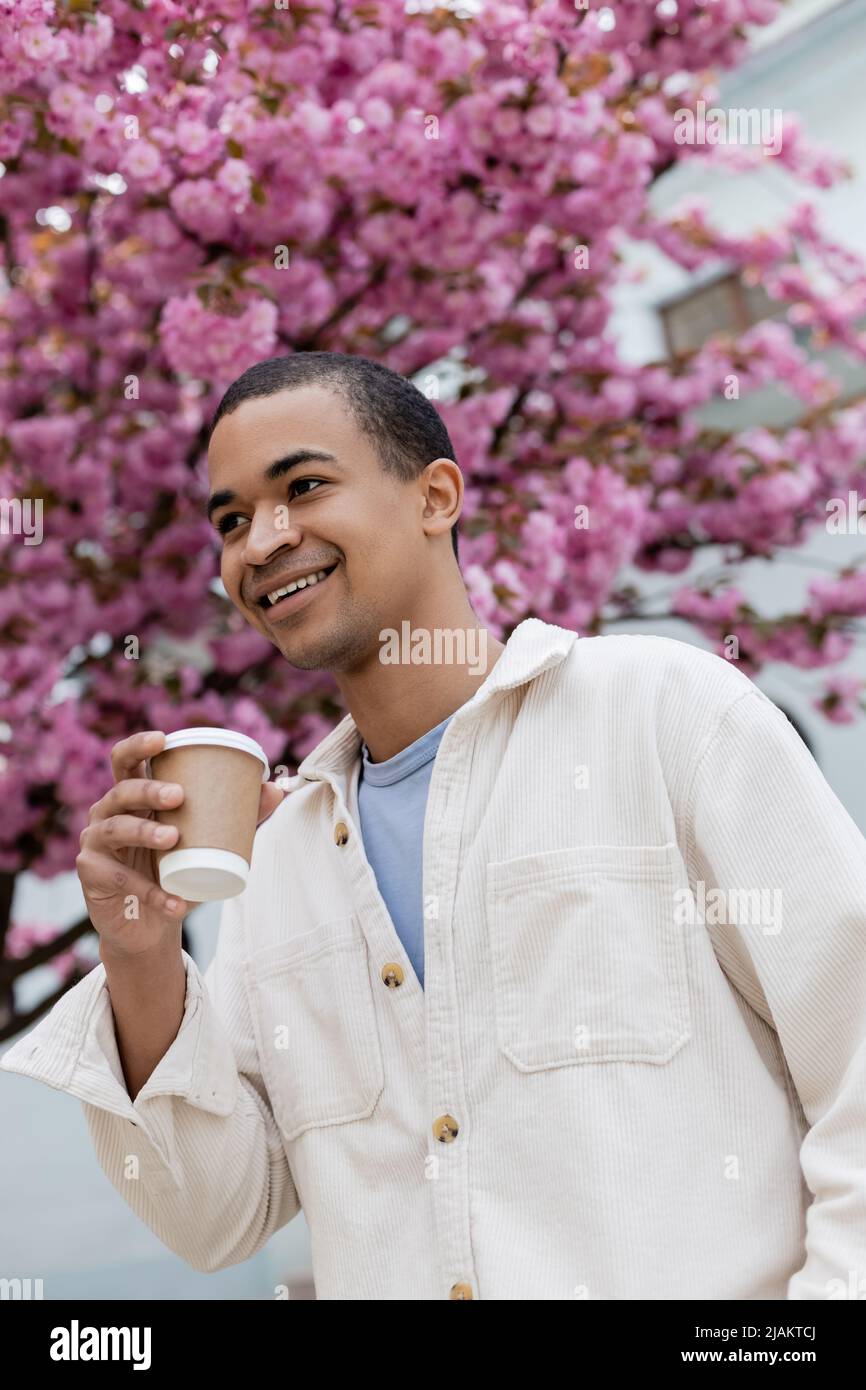 low angle view of happy african american man holding coffee to go near ...