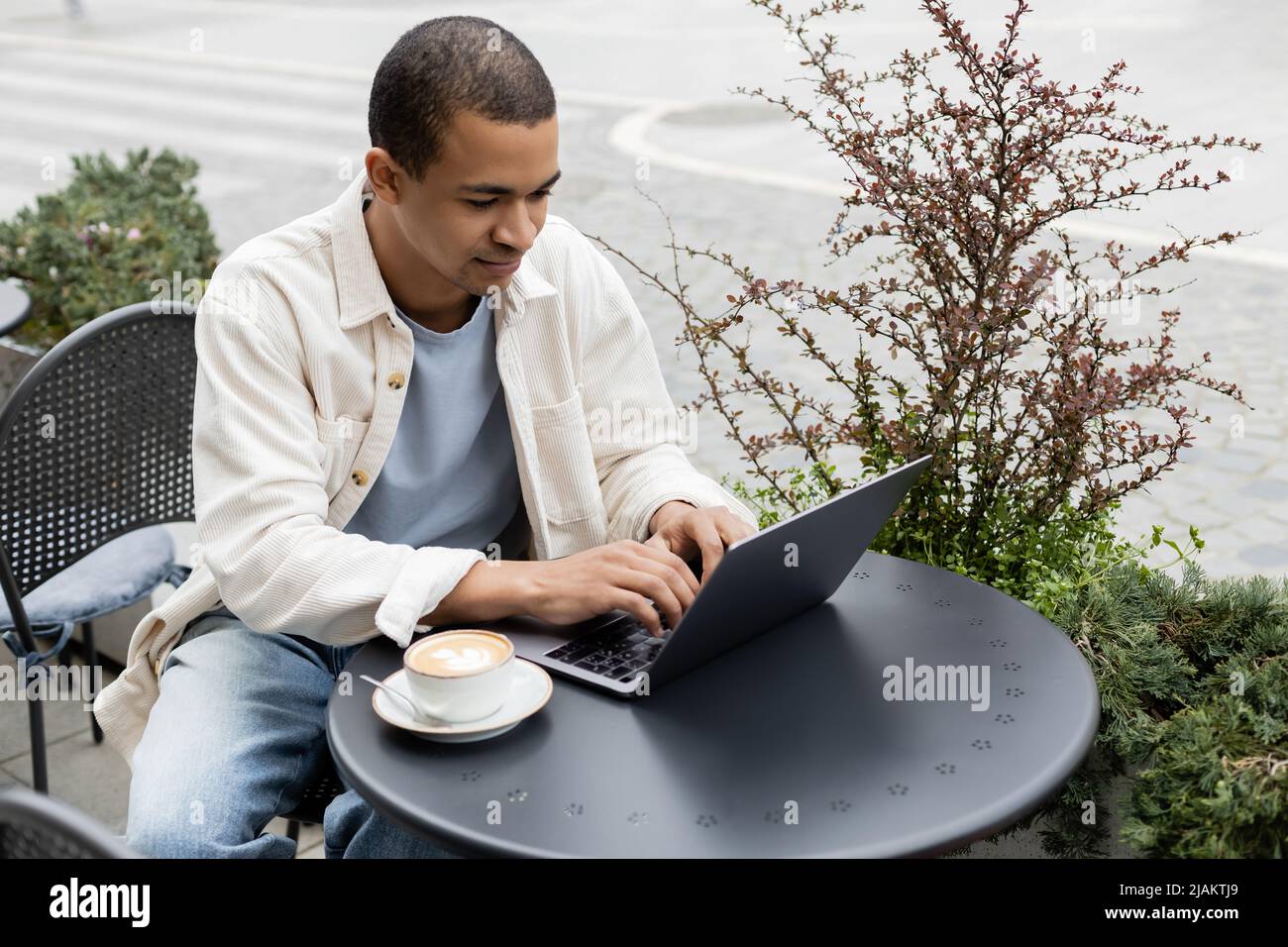 african american man using laptop near cup of latte with foam on table ...