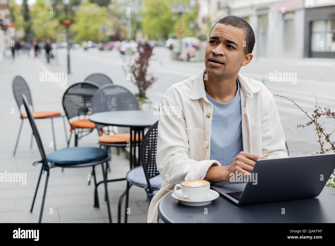 distracted african american freelancer looking away near laptop and cup ...