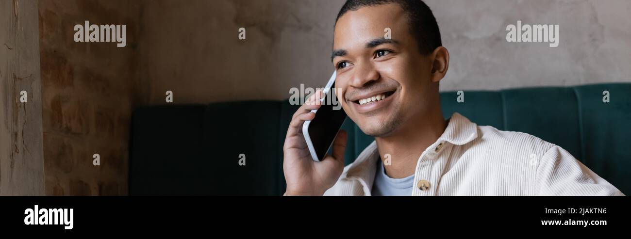 smiling and young african american man talking on smartphone in coffee ...