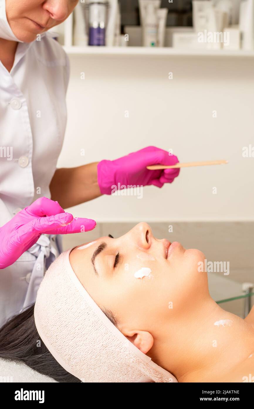 Cosmetologist with gloved hands applies a moisturizing mask with ...