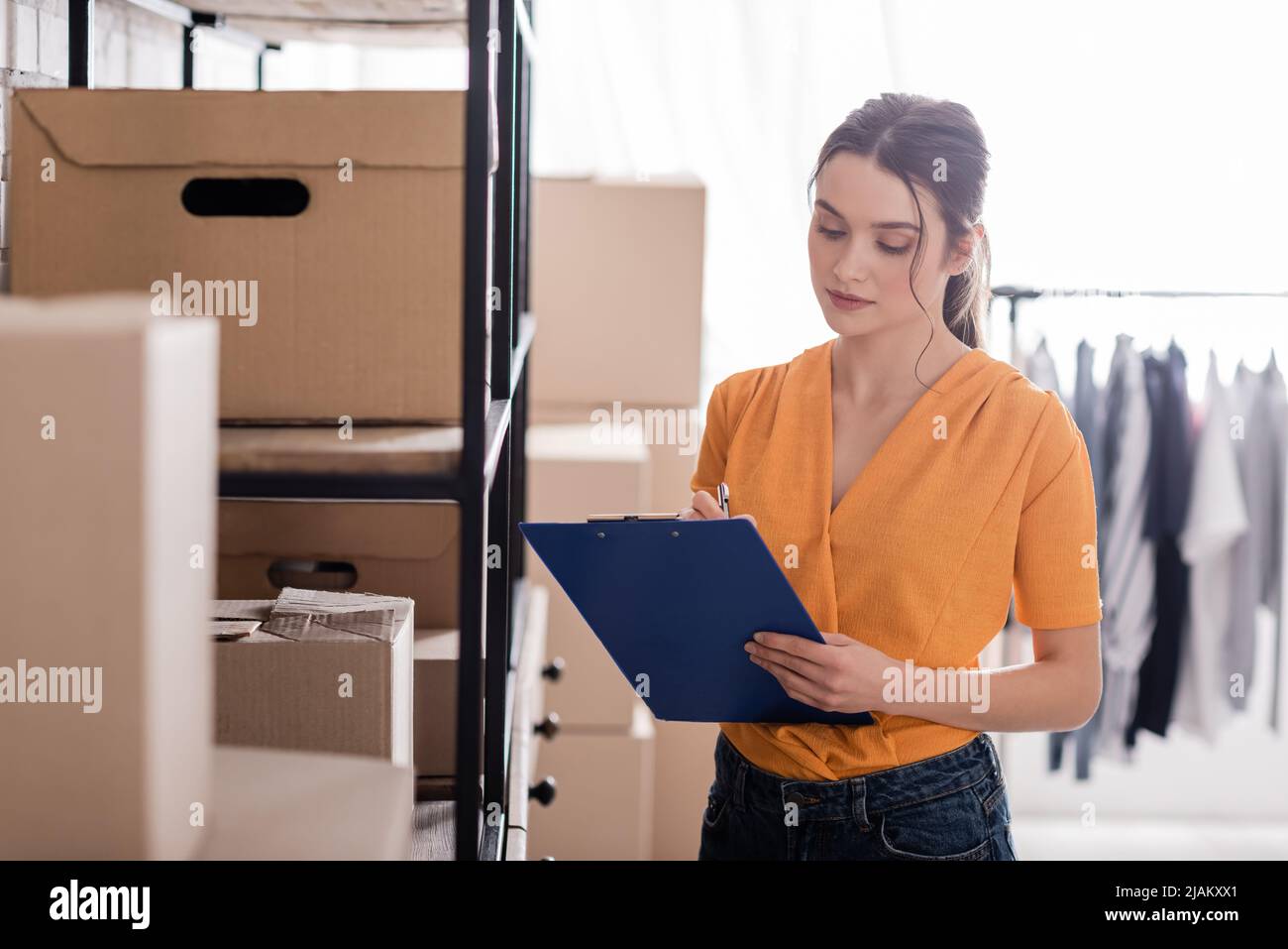 Owner of online web store writing on clipboard near carton boxes on ...