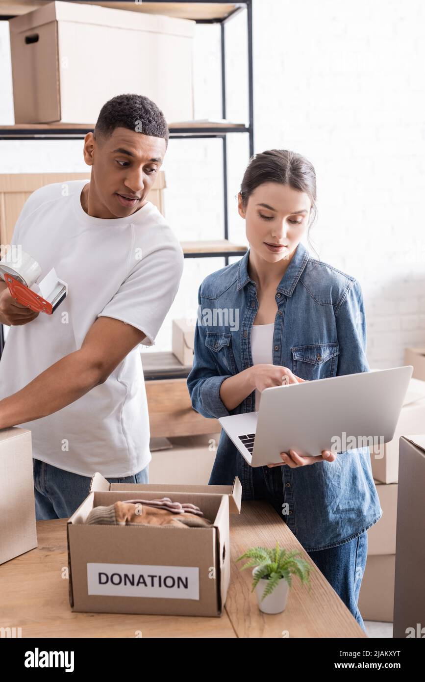 Seller holding laptop near african american colleague with adhesive ...