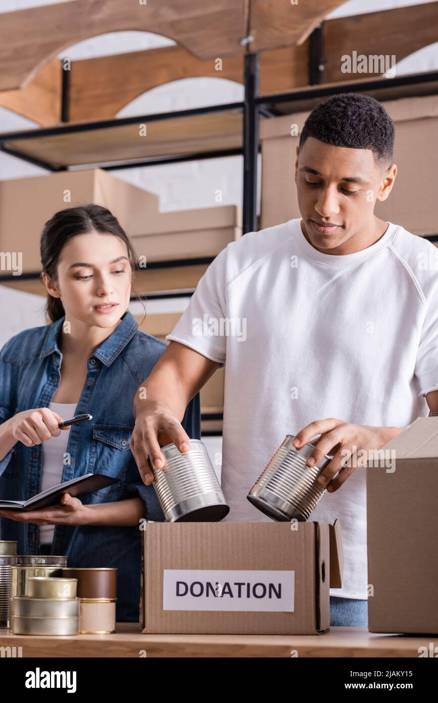 Multiethnic online web store owners packaging canned food in box with ...