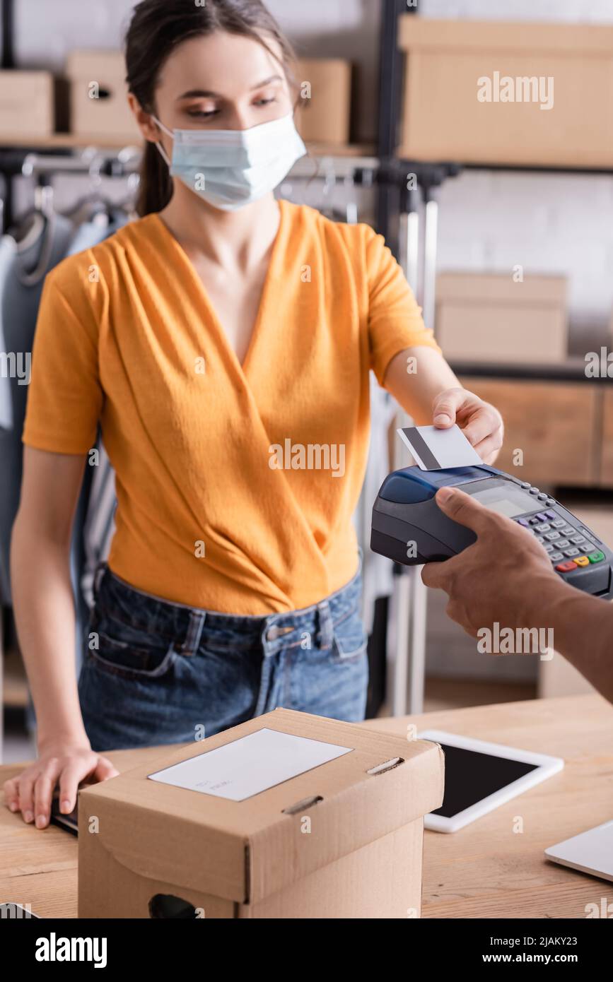 Seller in medical mask paying with credit card near african american ...