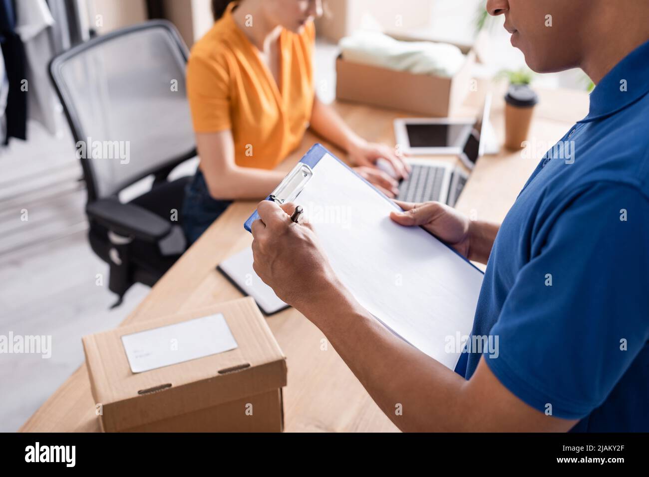 Cropped view of african american courier writing on clipboard in online ...