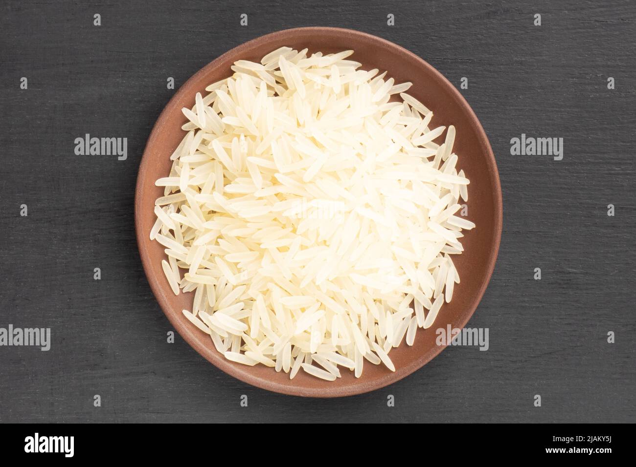 Long Basmati rice in clay plate on black wooden background. Macro. Flat ...