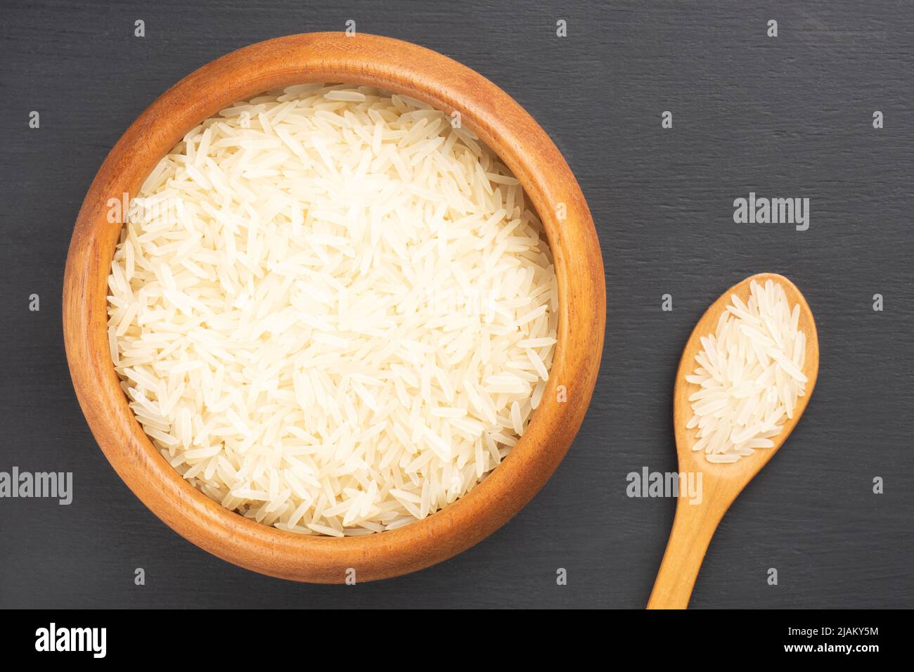 Long Basmati rice in wooden bowl and spoon on black background. Macro ...