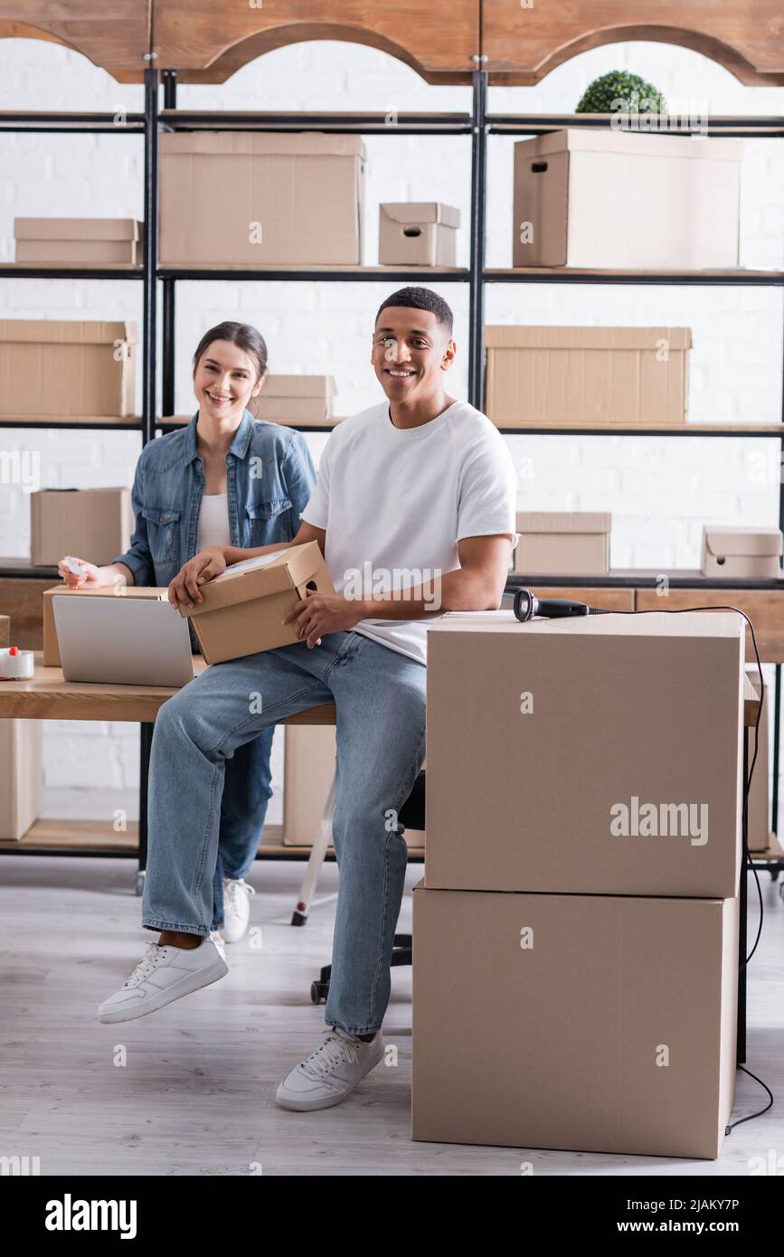 Positive multiethnic online web store owners looking at camera near ...