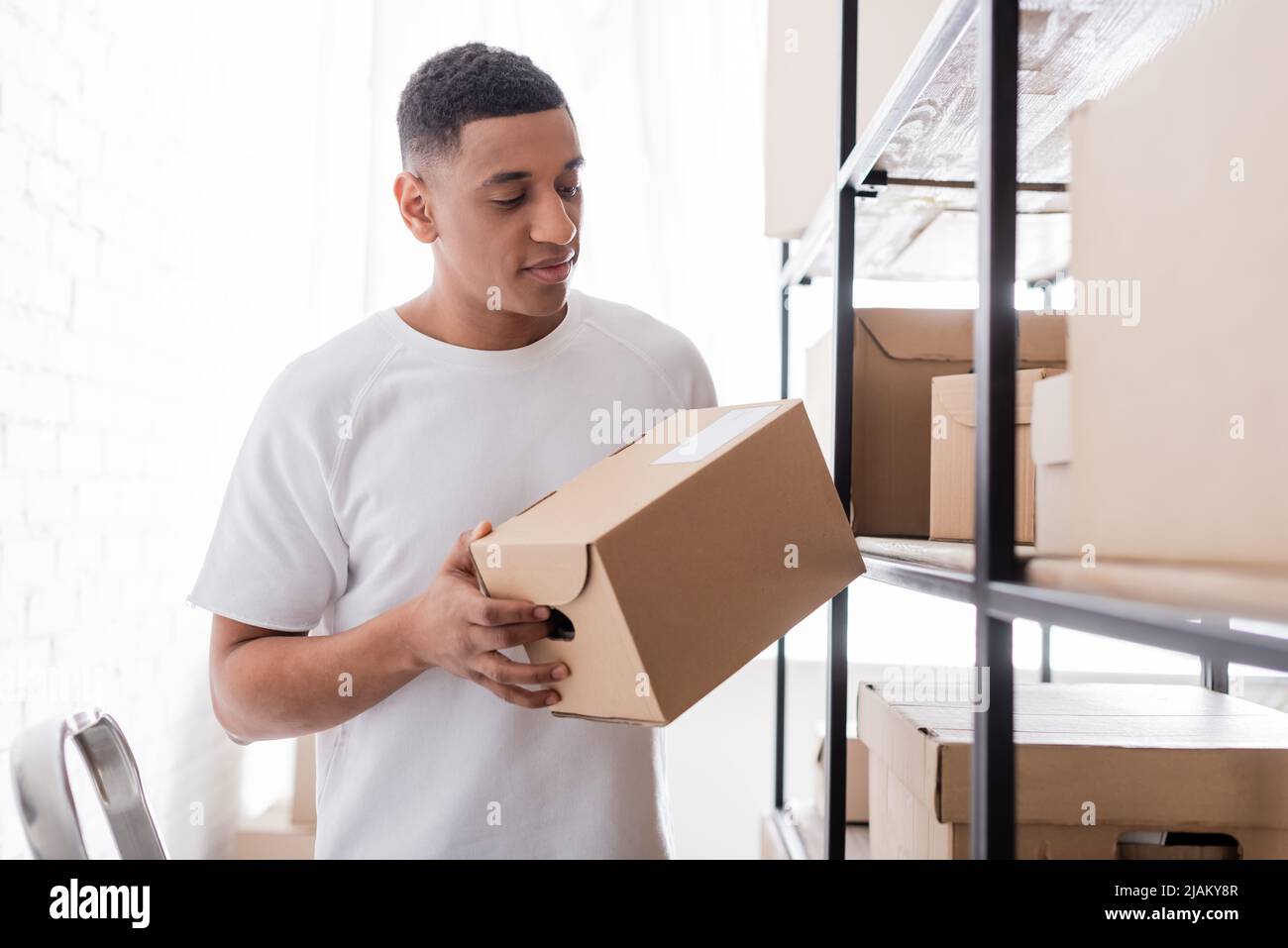 African american seller holding package near rack in online web store ...