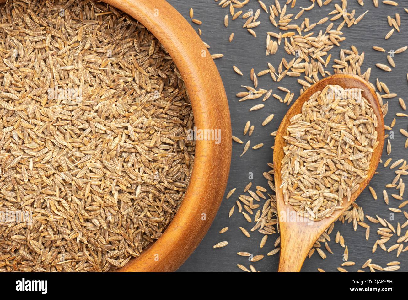 Spice cumin (jeera) in wooden bowl, spoon and bunch on black wooden ...