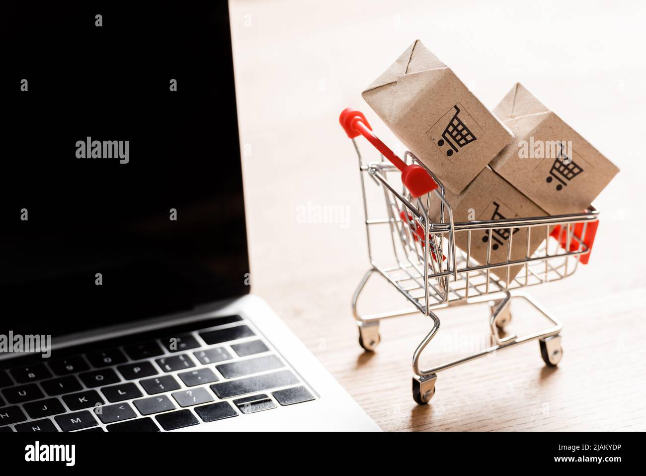 Packages in toy shopping cart near laptop with blank screen on table ...
