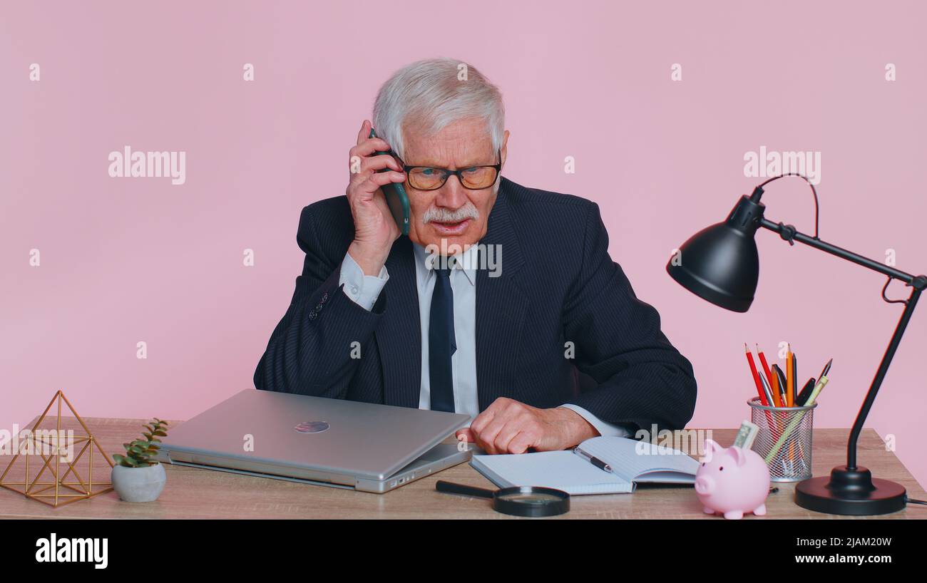 Angry senior business man making phone call at pink office work place ...