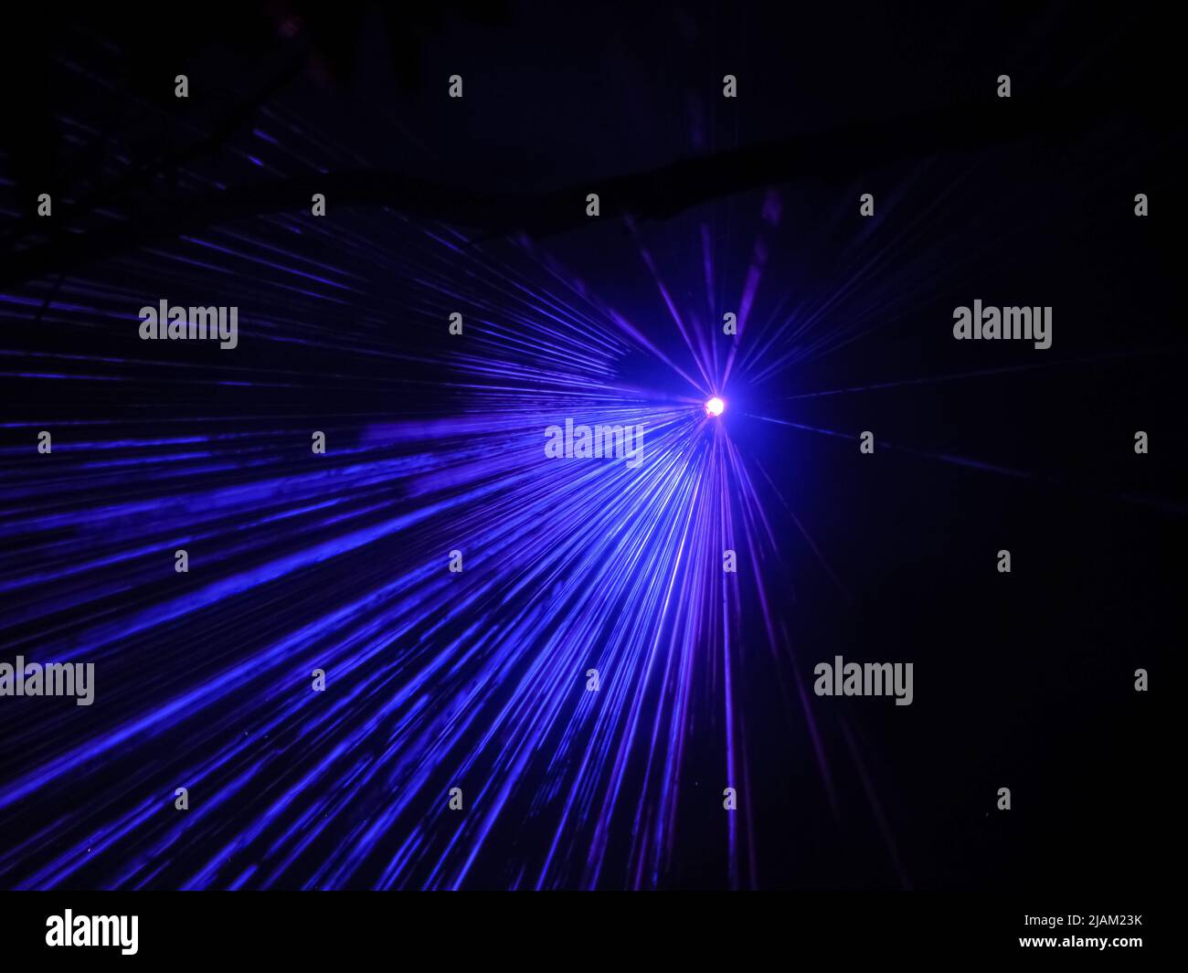 A bright spotlight projects neon blue beams in dark night space. Laser ...